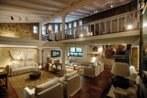 Amplo espaço de estar estilo loft, com teto alto, paredes de pedra e varanda.