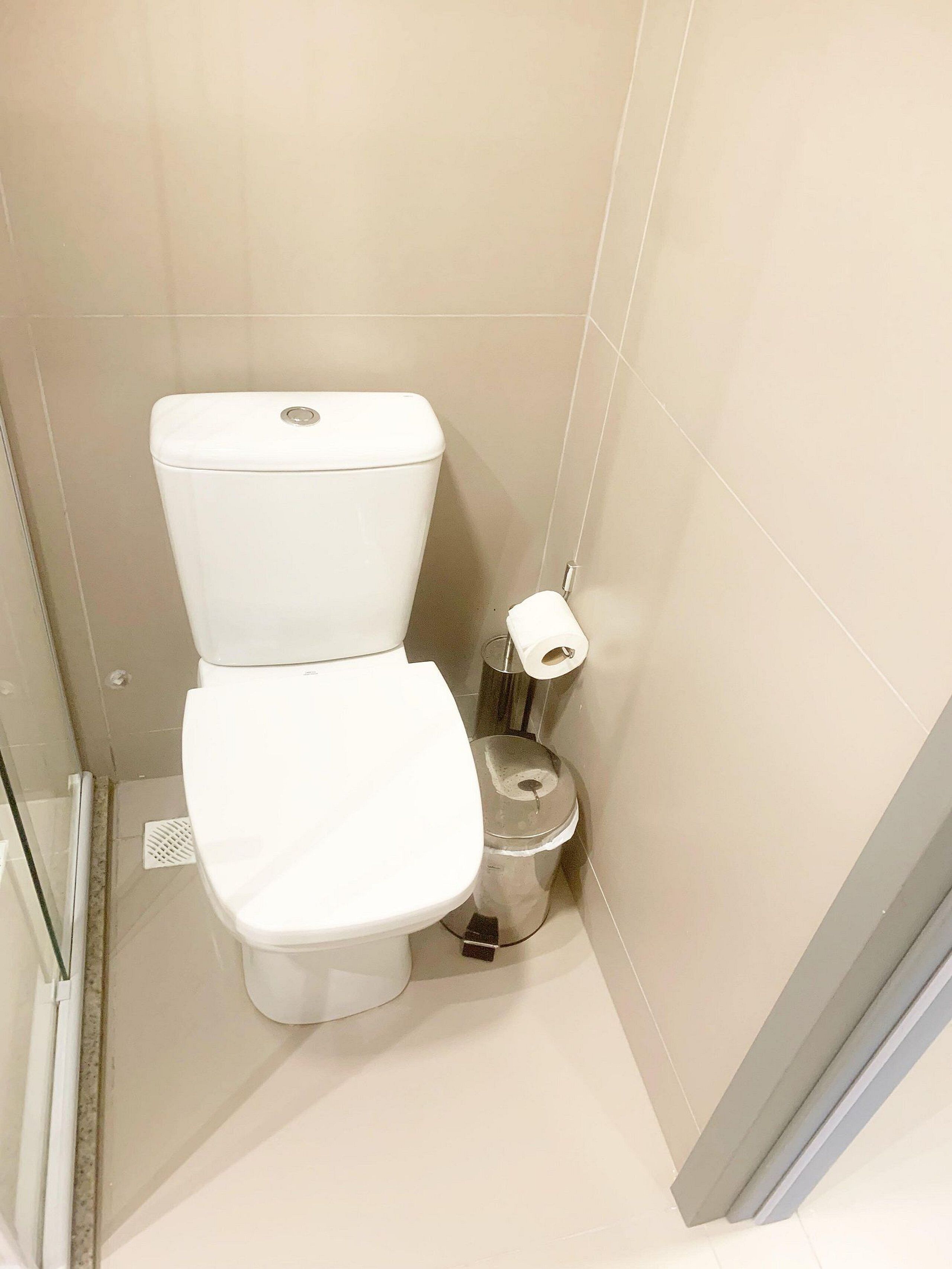 Uma casa de banho pequena e moderna, com uma sanita branca, um lixo e um rolo de papel higiénico.