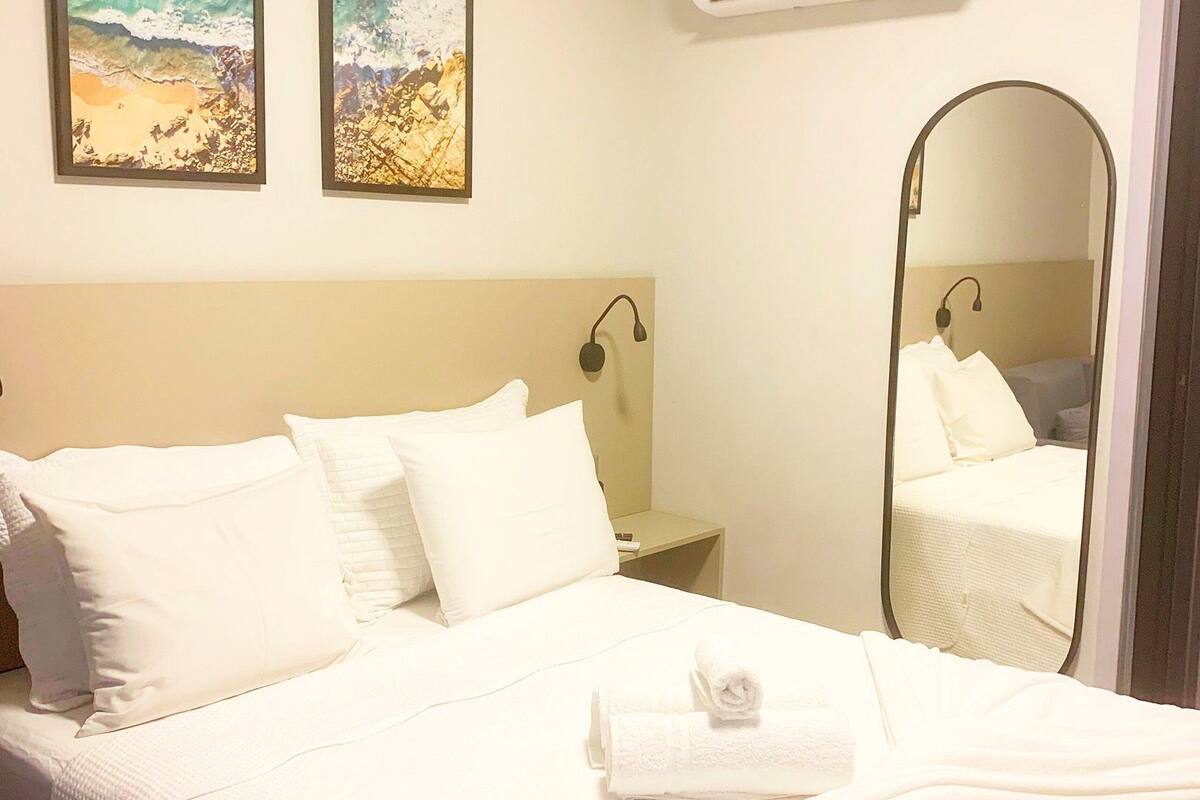 Quarto de hotel com cama, mesa de cabeceira, espelho e duas pinturas penduradas na parede.