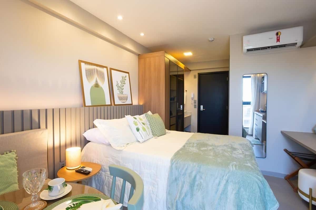 Quarto de hotel com cama, mesa de cabeceira, abajur e espelho.