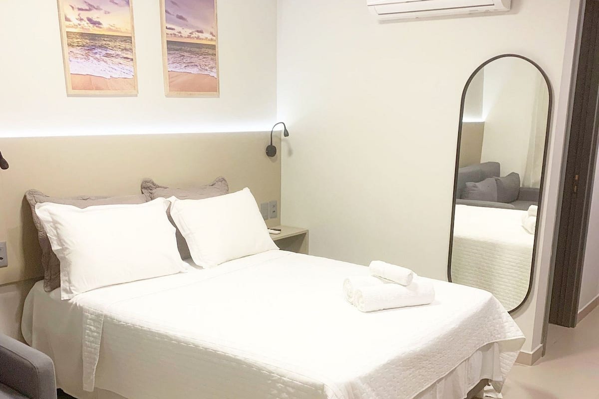 Quarto com cama, mesa de cabeceira, ar condicionado fixado na parede e duas fotos emolduradas.