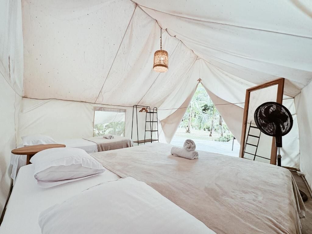 Alojamento em tenda com duas camas, uma luminária pendente e um ventilador.