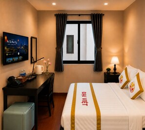 Quarto de hotel com cama, escrivaninha, televisão e janela com cortinas.