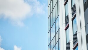 Um edifício alto com fachada de vidro moderna e céu claro com nuvens.