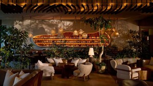 Uma área de bar com prateleiras de garrafas, luminárias pendentes e assentos com plantas.