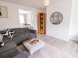 Uma sala de estar moderna com um sofá seccional cinza, um banquinho pequeno com uma cesta, uma estante de madeira e um espelho redondo na parede.