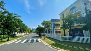 Rua arborizada com cerca branca, levando a um edifício com varanda e uma placa com o texto 'Wonder 7 Street'.