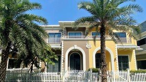 Um edifício de dois andares com cerca branca de piquete, uma entrada central em arco e uma varanda no andar superior.