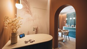 Um lobby de hotel moderno com uma mesa de recepção, um vaso com flores secas e vista para a área de refeições.