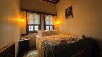 Quarto com cama, mesa de cabeceira, abajur e janela com cortinas.