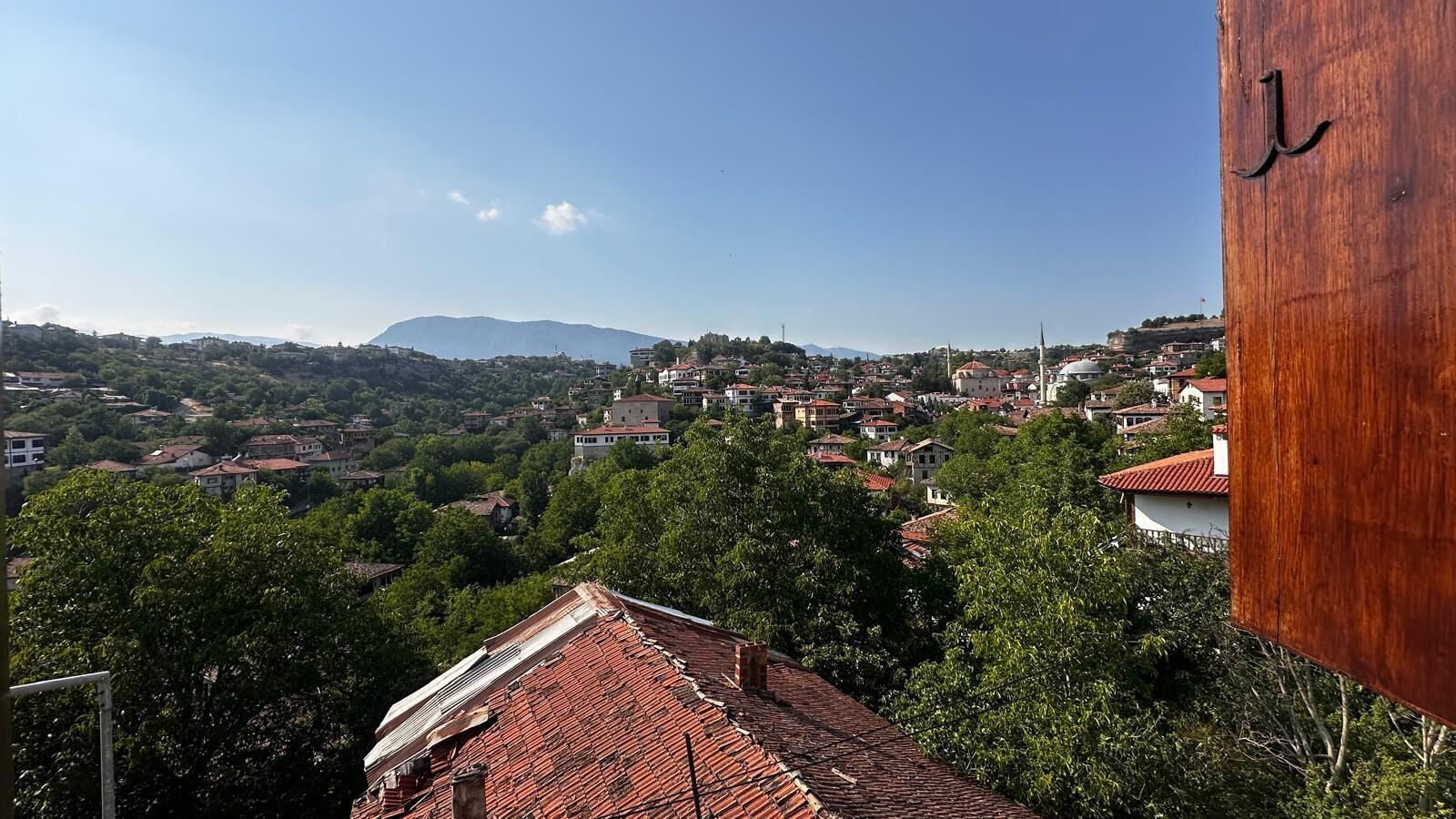 Uma cidade com telhados de cerâmica vermelha, vegetação densa e uma montanha ao fundo.