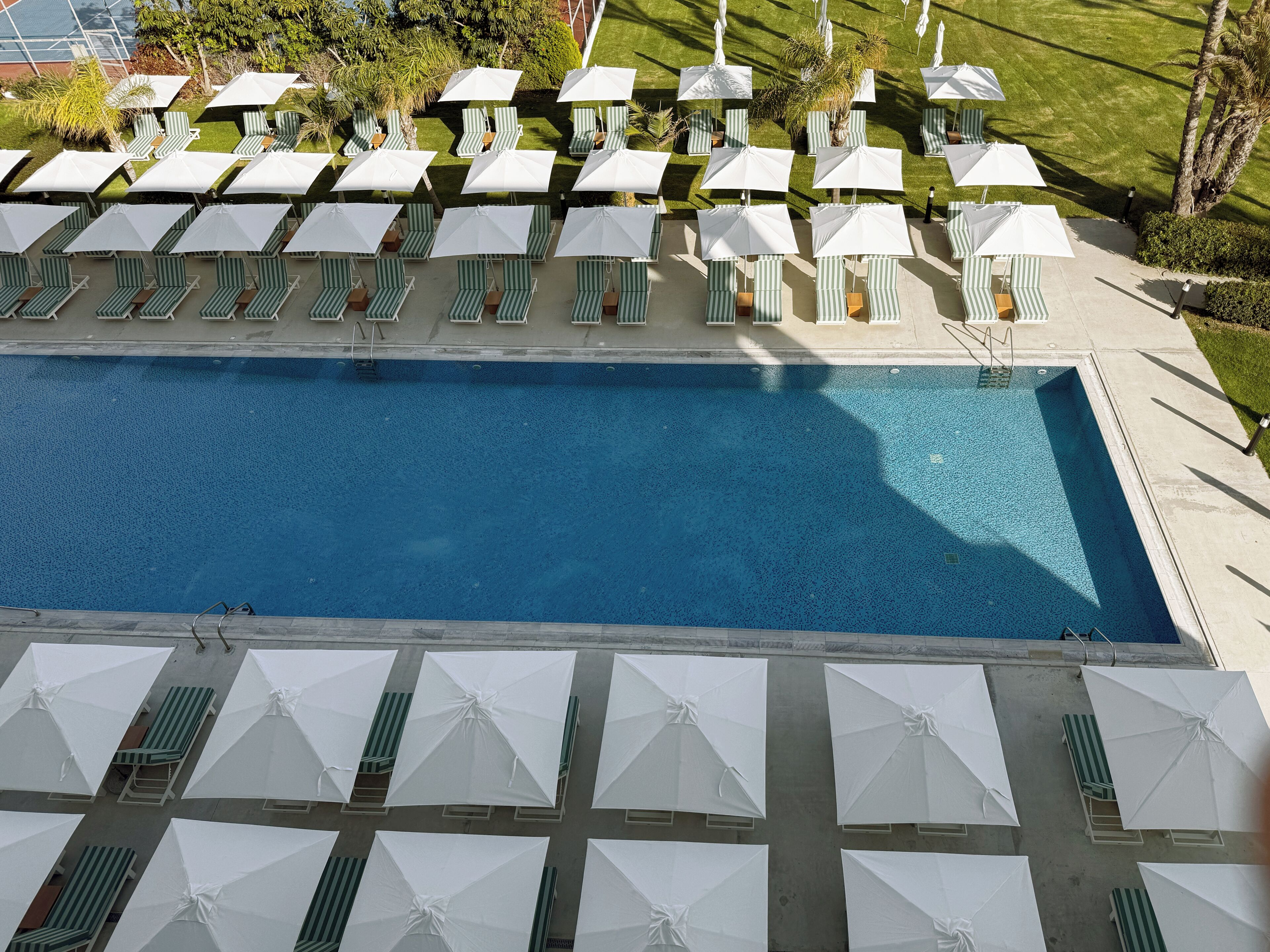 Uma área de piscina com espreguiçadeiras e guarda-sóis dispostos ao redor da piscina.
