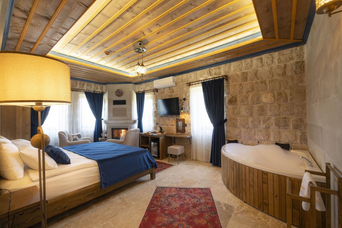 Quarto com cama grande, escrivaninha, lareira, parede de pedra e banheira.