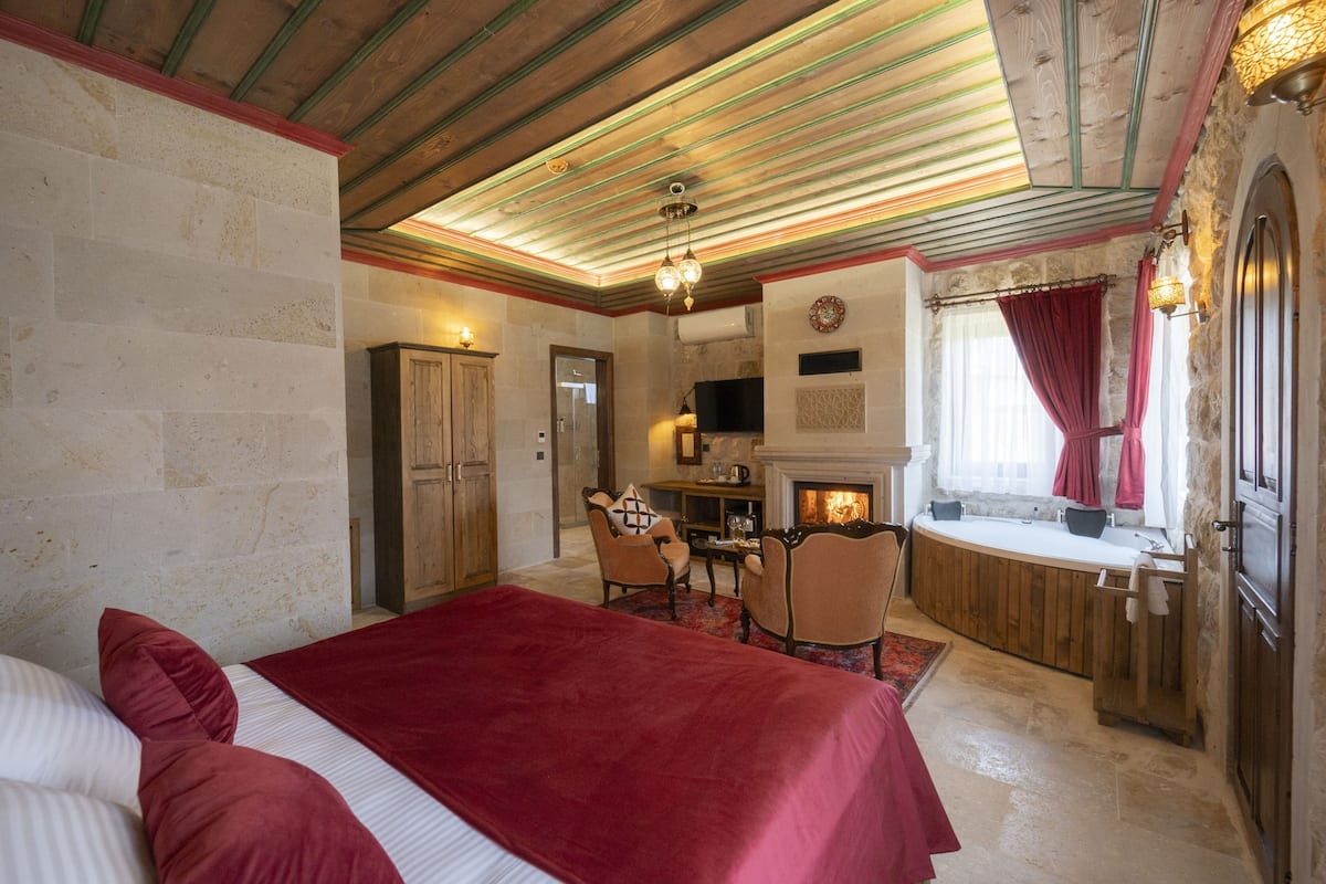 Um quarto com uma cama grande, teto de madeira, lareira e um espaço de refeições com cadeiras e uma mesa.