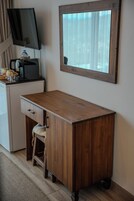Uma secretária de madeira com uma cadeira, uma televisão e uma janela com cortinas.