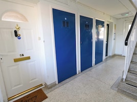 Um corredor com portas brancas e uma porta azul, um tapete de entrada e uma escadaria.