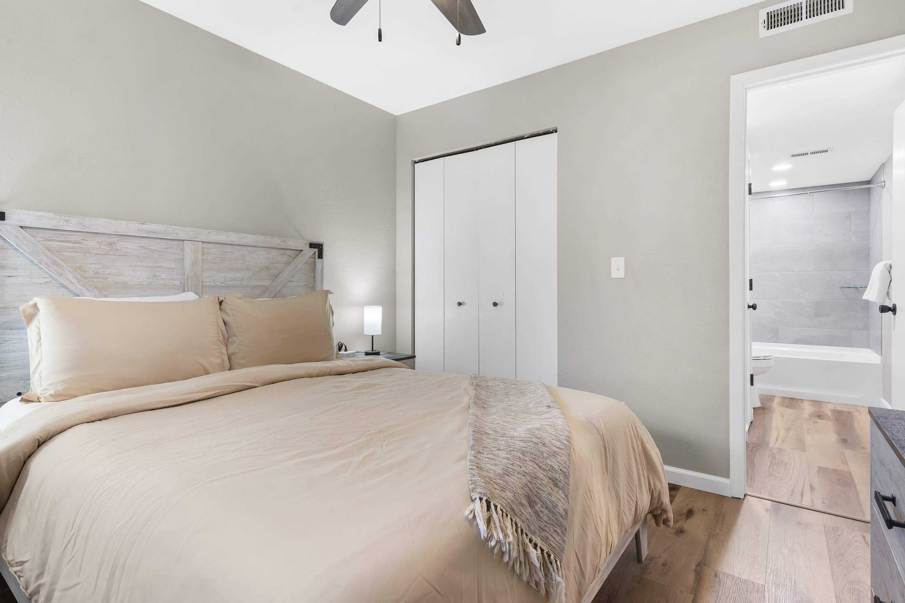 Quarto com cama, mesas de cabeceira, guarda-roupa e banheiro com chuveiro e vaso sanitário.