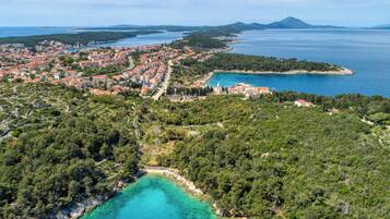 Vista aérea de uma vila costeira com uma baía turquesa translúcida, áreas florestais verdes e densas, e uma igreja imponente.