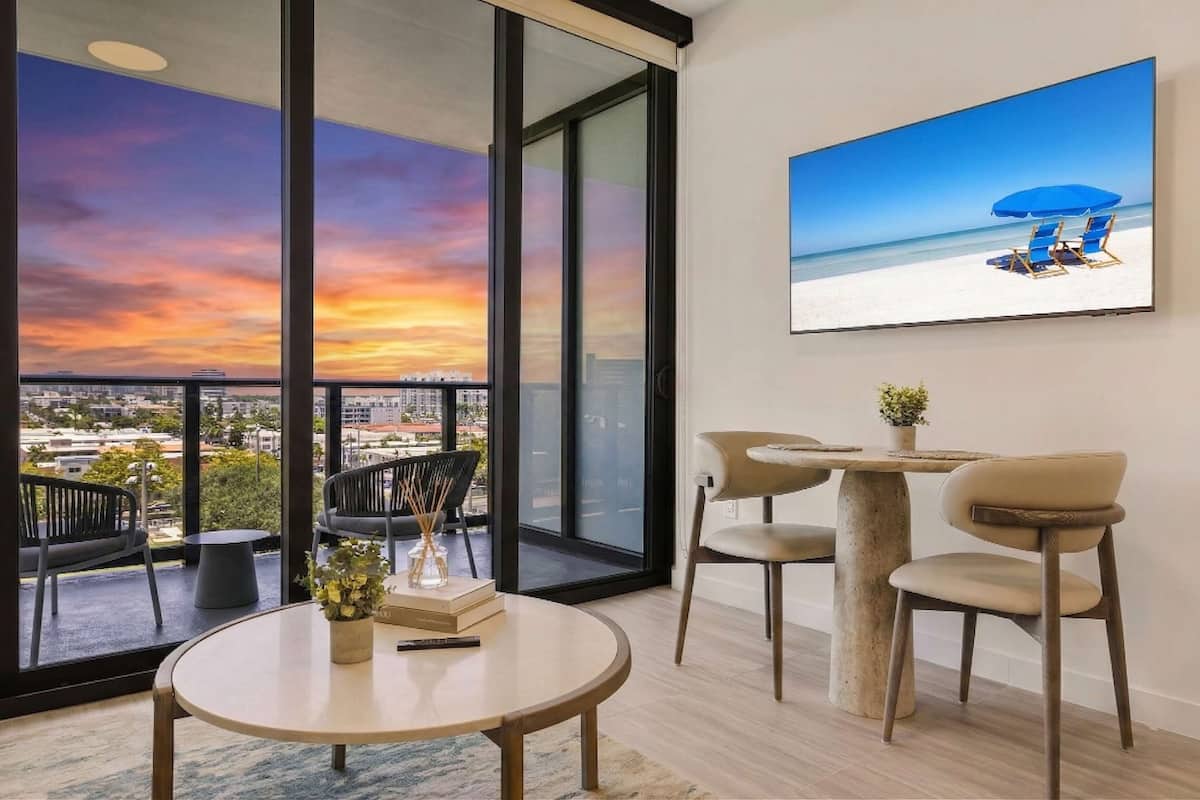 Uma varanda com vista para a cidade, uma mesa com cadeiras e um quadro de uma cena de praia.