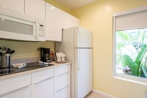 Cozinha com armários brancos, micro-ondas, geladeira e janela com vista para o verde.