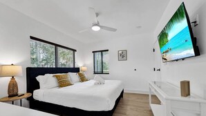 Quarto moderno com cama, mesas de cabeceira, ventilador de teto, TV e janelas amplas.