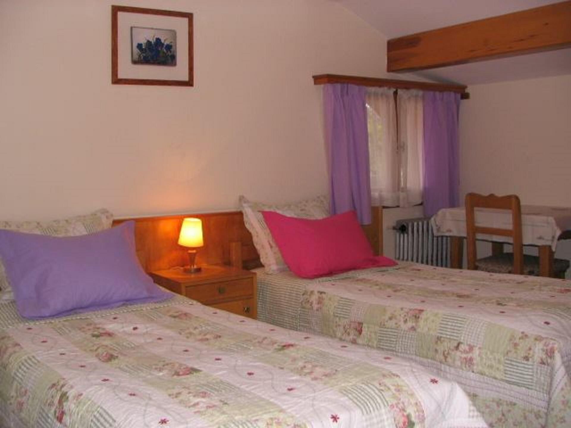 Quarto com duas camas, mesa de cabeceira, cadeira e radiador.
