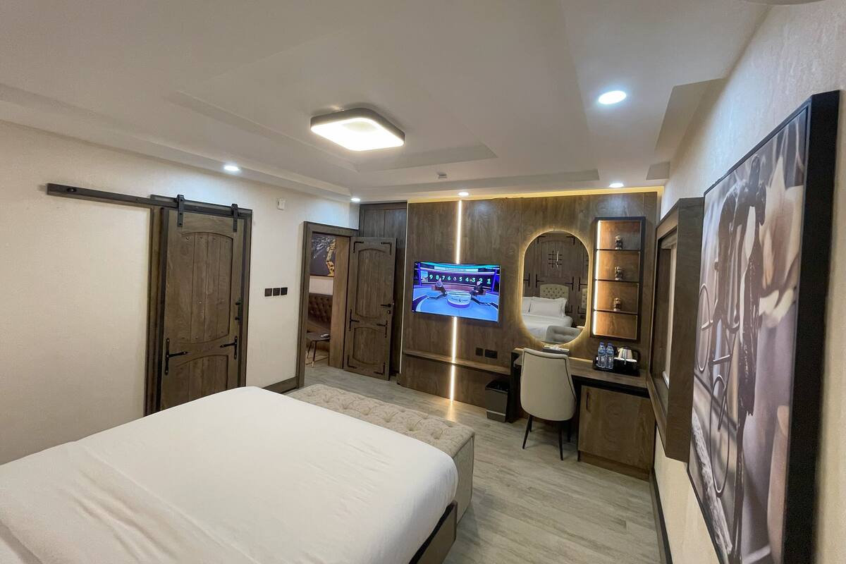 Quarto de hotel com cama, escrivaninha, televisão e espelho.