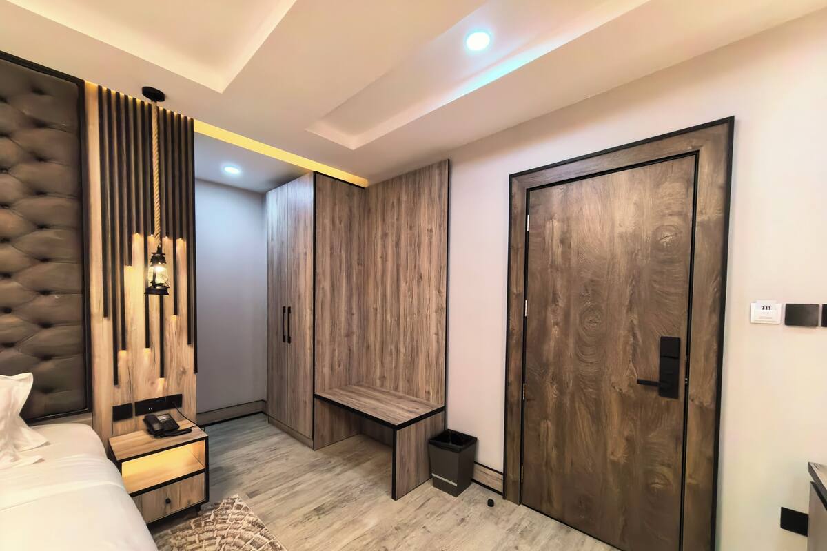 Quarto moderno com cabeceira estofada, guarda-roupa de madeira, mesa de cabeceira e um pequeno banco.