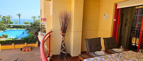 Varanda com vista para a piscina, mesa de jantar posta com pratos e copos, e um vaso decorativo.
