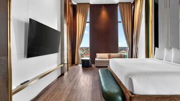 Quarto de hotel moderno com uma cama grande, um banco, um sofá e uma TV fixada na parede.