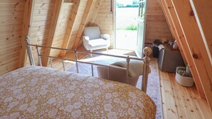 Uma cabana de madeira com quarto no mezanino, um pequeno espaço de estar e uma porta que dá para o exterior.