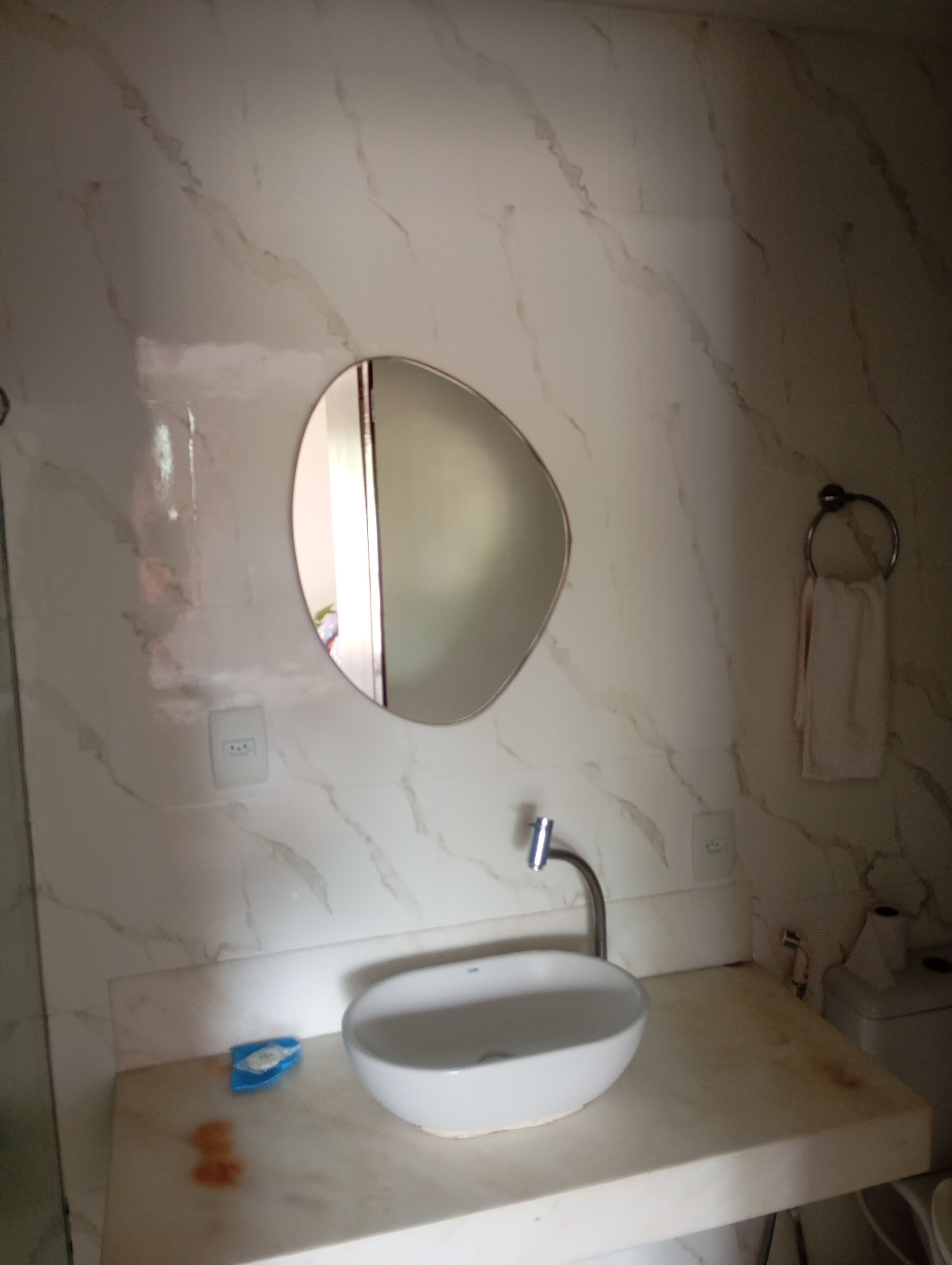 Casa de banho com lavatório de mármore branco, espelho redondo e porta-toalhas.