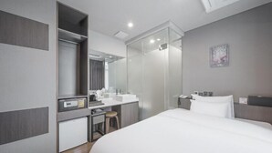 Quarto de hotel moderno com uma cama grande, uma escrivaninha com computador, um espelho e área de chuveiro.