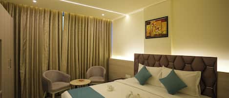 Quarto de hotel com cama, duas cadeiras, uma mesinha e um ventilador de teto.