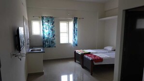 Quarto com cama, uma mesinha, pia e janela com cortinas.