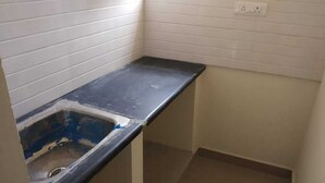 Cozinha pequena e inacabada, com pia, paredes revestidas de azulejos brancos e bancada preta.