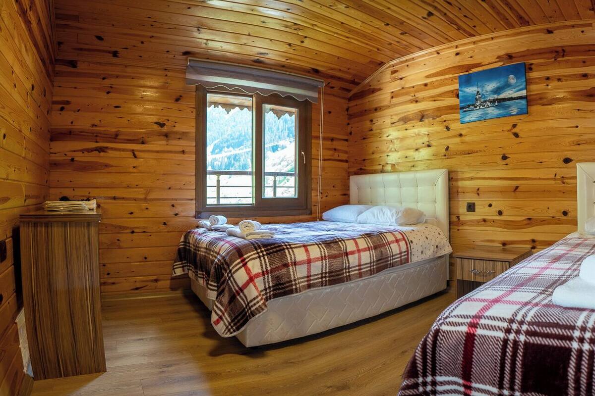 Quarto de cabana de madeira com duas camas, uma janela e um quadro na parede.
