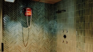 Casa de banho com padrão de tijolos em herringbone, um banco de madeira e zona de duche com porta de vidro.