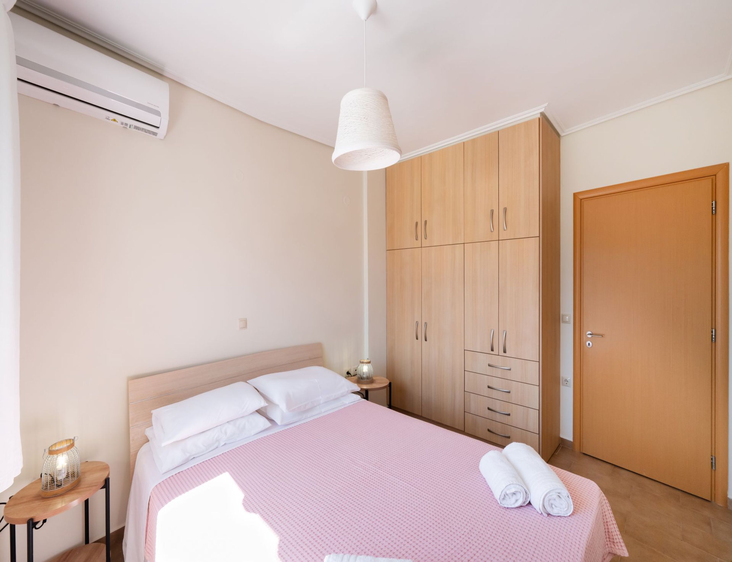 Quarto com cama, mesa de cabeceira, luminária, guarda-roupa e ar condicionado.