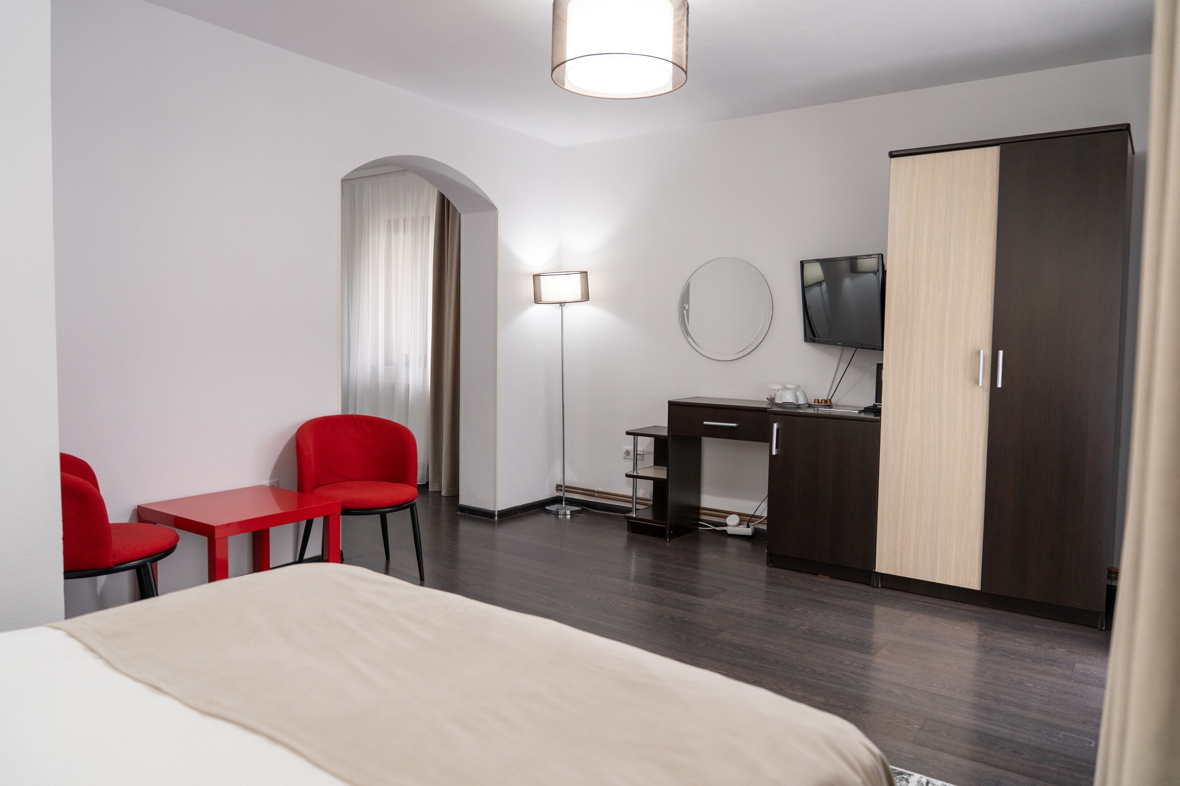 Quarto de hotel com cama, escrivaninha, cadeira, guarda-roupa, televisão e abajur.