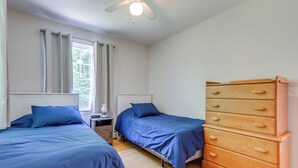 Quarto com duas camas, uma cômoda de madeira e um ventilador de teto.