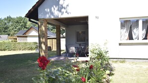 Uma casa com varanda coberta, gramado e jardim com flores vermelhas.