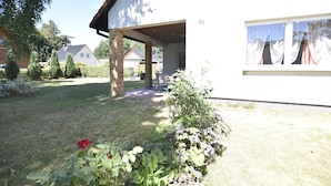 Uma casa moderna com varanda coberta, gramado bem cuidado e jardim com flores vermelhas.