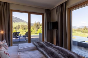 Quarto de hotel com uma cama grande, televisão e varanda com vista para um campo de golfe e montanhas.