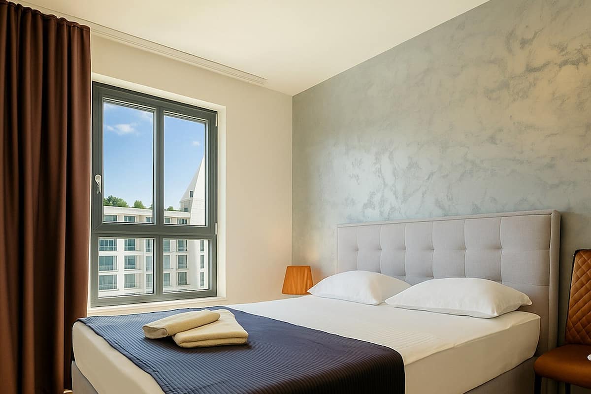 Quarto de hotel com uma cama grande, vista de edifícios pela janela e uma cadeira.