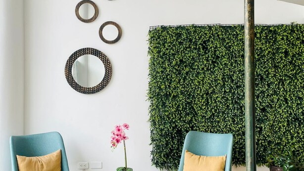 Uma sala de estar moderna com dois poltronas verde-água, uma mesinha lateral, um espelho decorativo, um painel de parede verde e um vaso com planta.