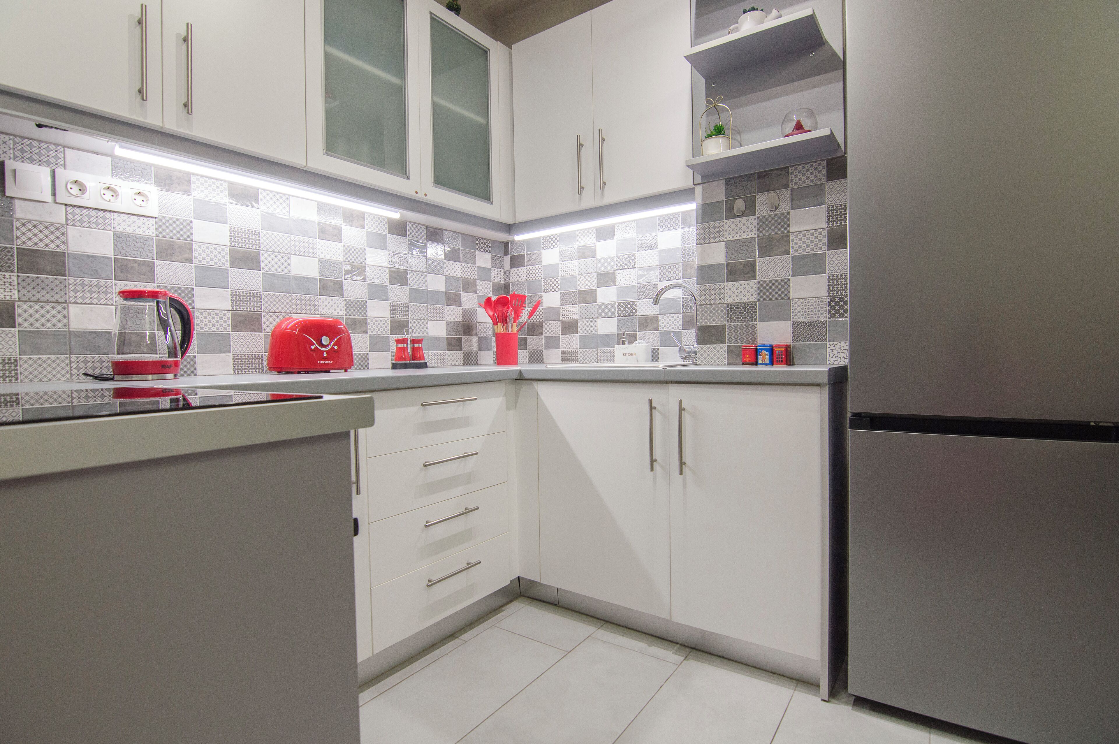 Cozinha moderna com armários brancos, geladeira de aço inoxidável e painel de fundo xadrez.