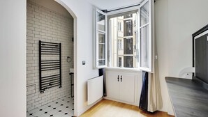 Quarto de canto com janela saliente, paredes com azulejos brancos, radiador e soalho de madeira.