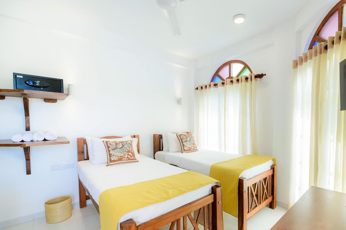 Quarto de hotel com duas camas, televisão, prateleira com artigos de higiene e janela com cortinas.