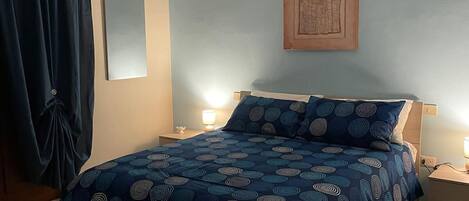 Quarto com cama, mesas de cabeceira, ar condicionado na parede, um quadro emoldurado e cortina.
